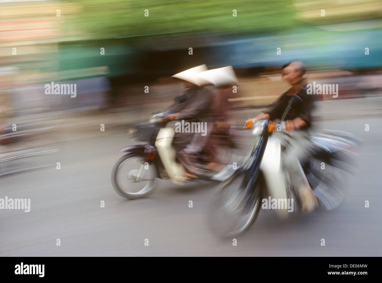 Two women in conical hats on a speeding mopeds in the Old Quarter ...