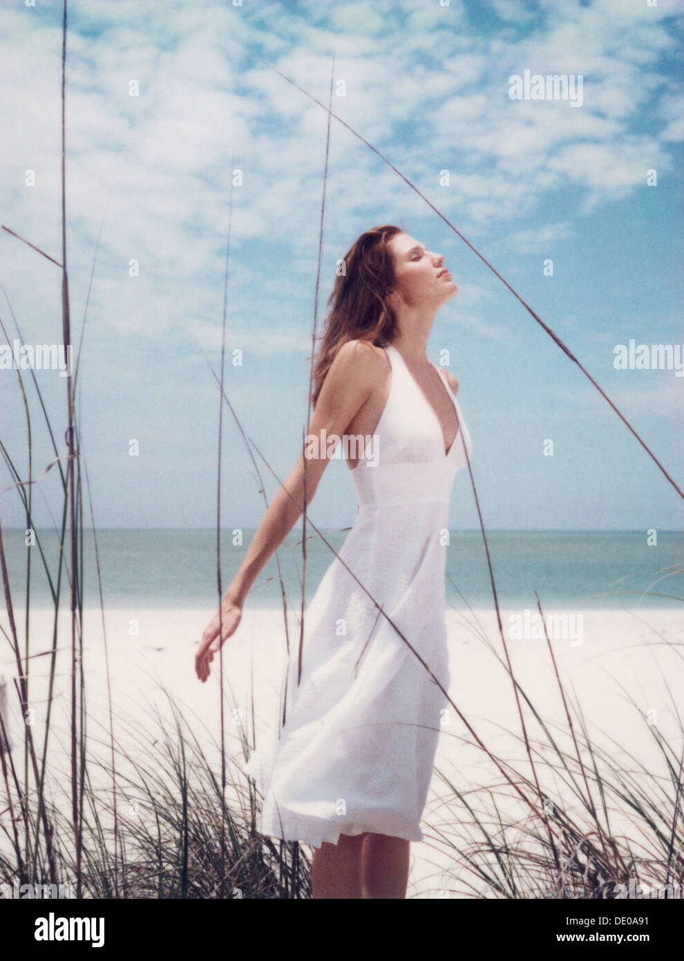 Young woman in dress standing in dune grass with head back, facing wind ...