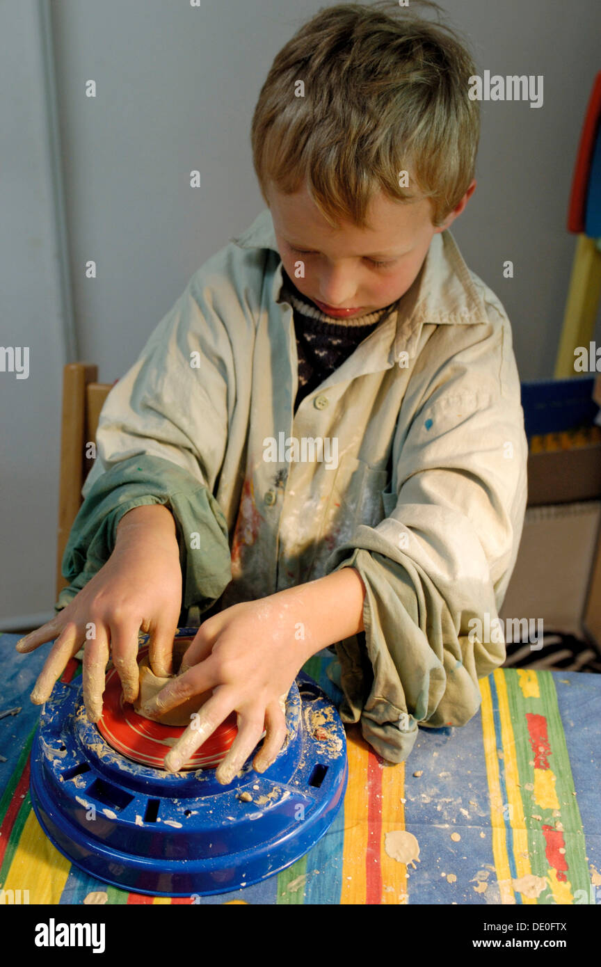 Little boy, 7, making pottery, turning a jar from clay on a potter's ...