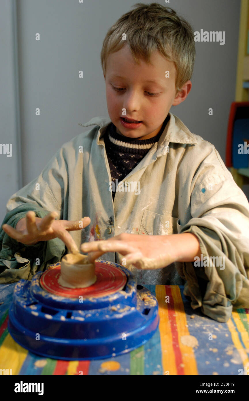 Little boy, 7, making pottery, turning a jar from clay on a potter's ...
