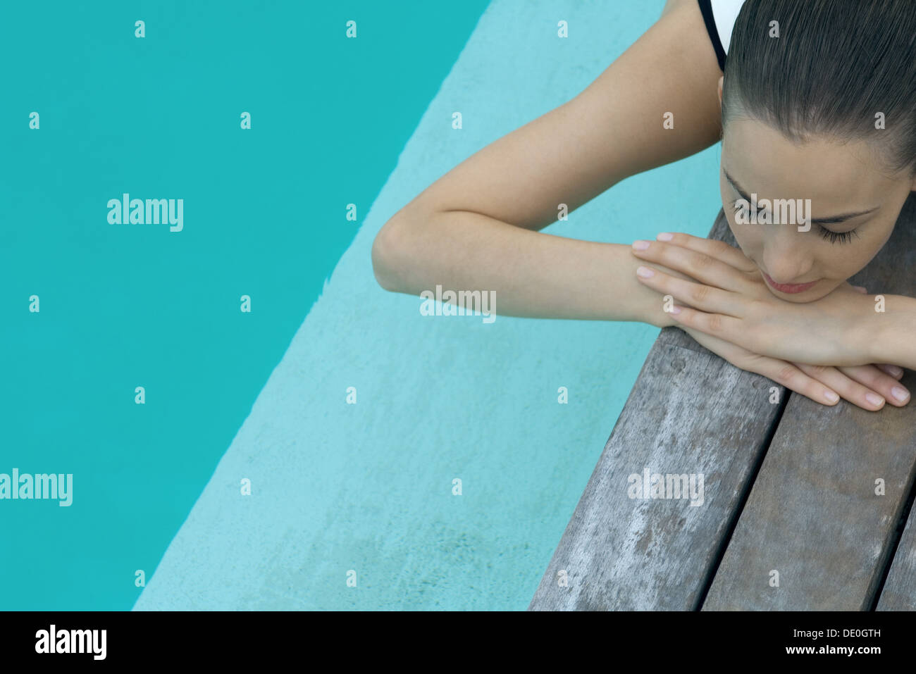 Woman lying on deck next to pool, resting head on arms, eyes closed ...