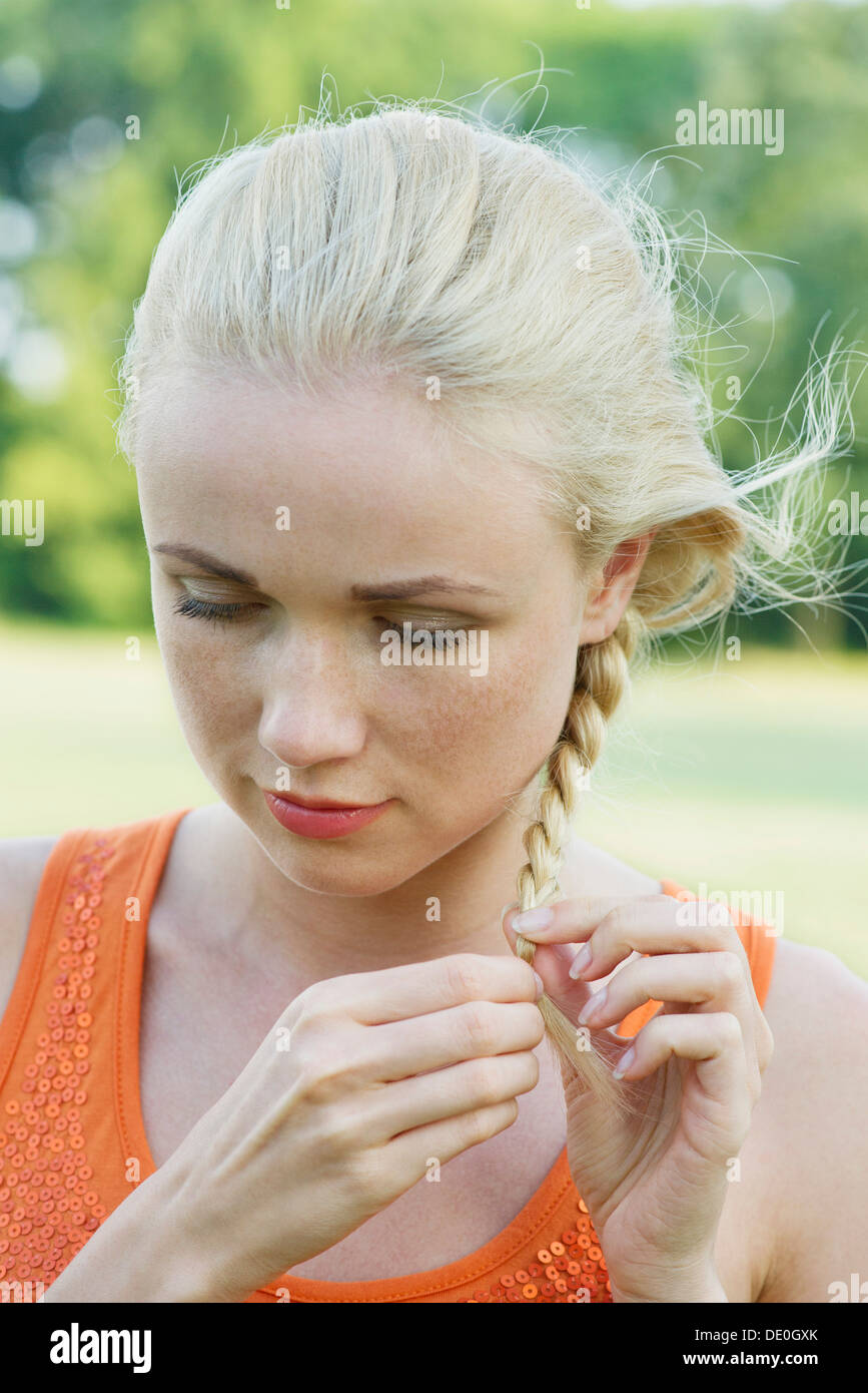 Young woman braiding hair, looking down in thought Stock Photo - Alamy
