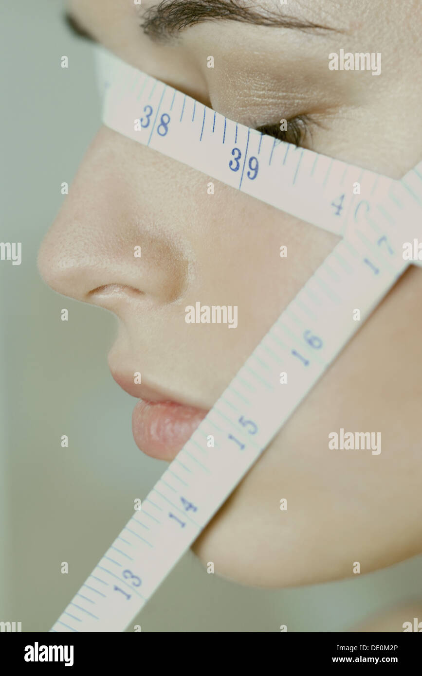 Woman with measuring tape wrapped across face, close-up Stock Photo - Alamy
