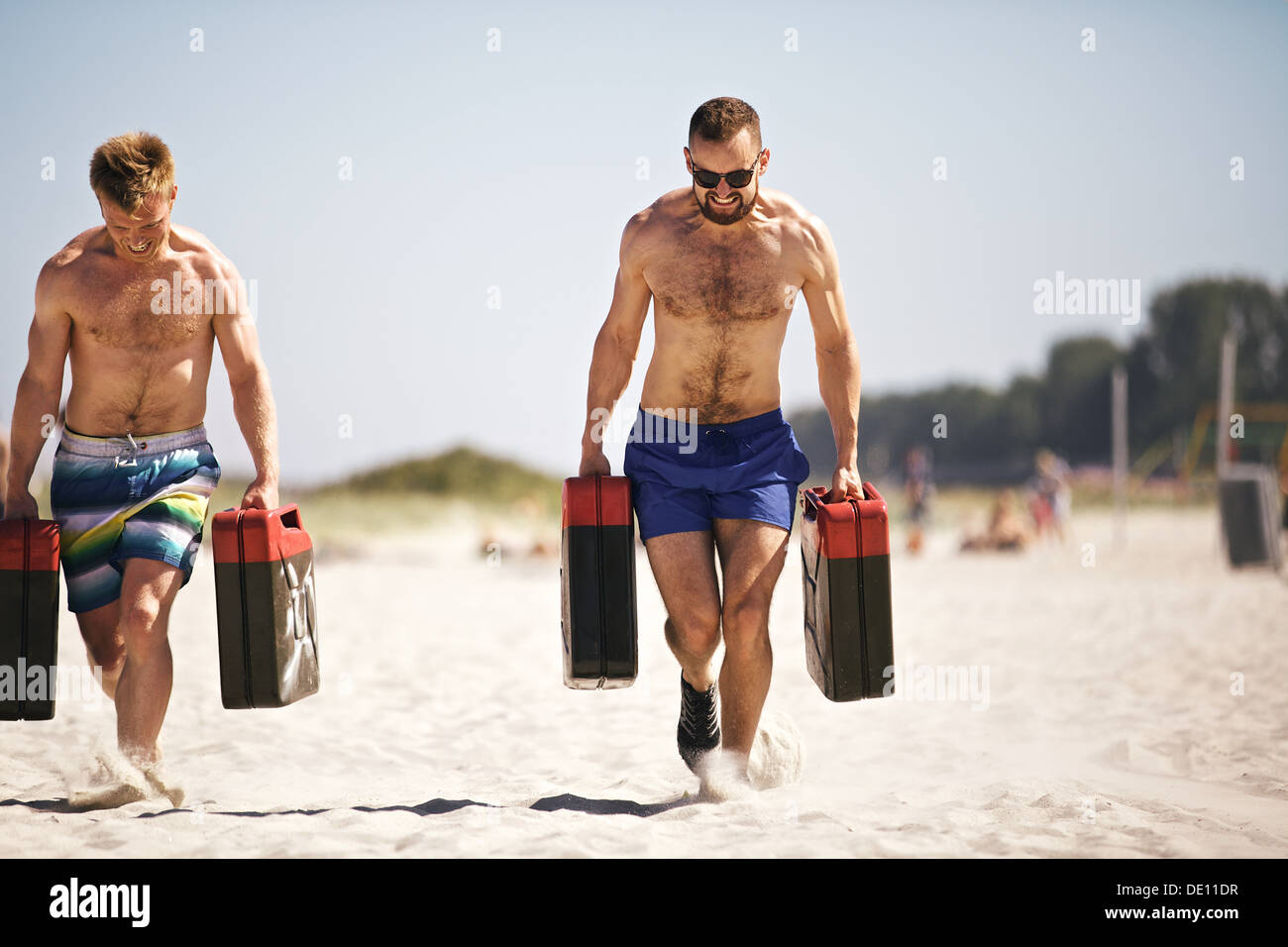 Strong crossfit guys lifting heavy jerrycans outside on beach. Muscular ...