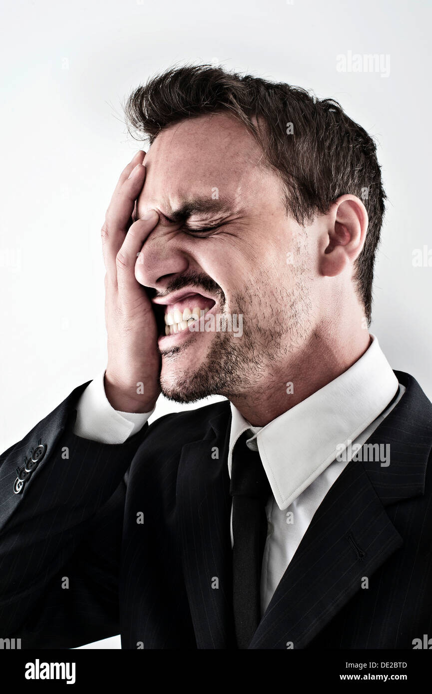 Desperate young man wearing a suit covering his face with his hand ...