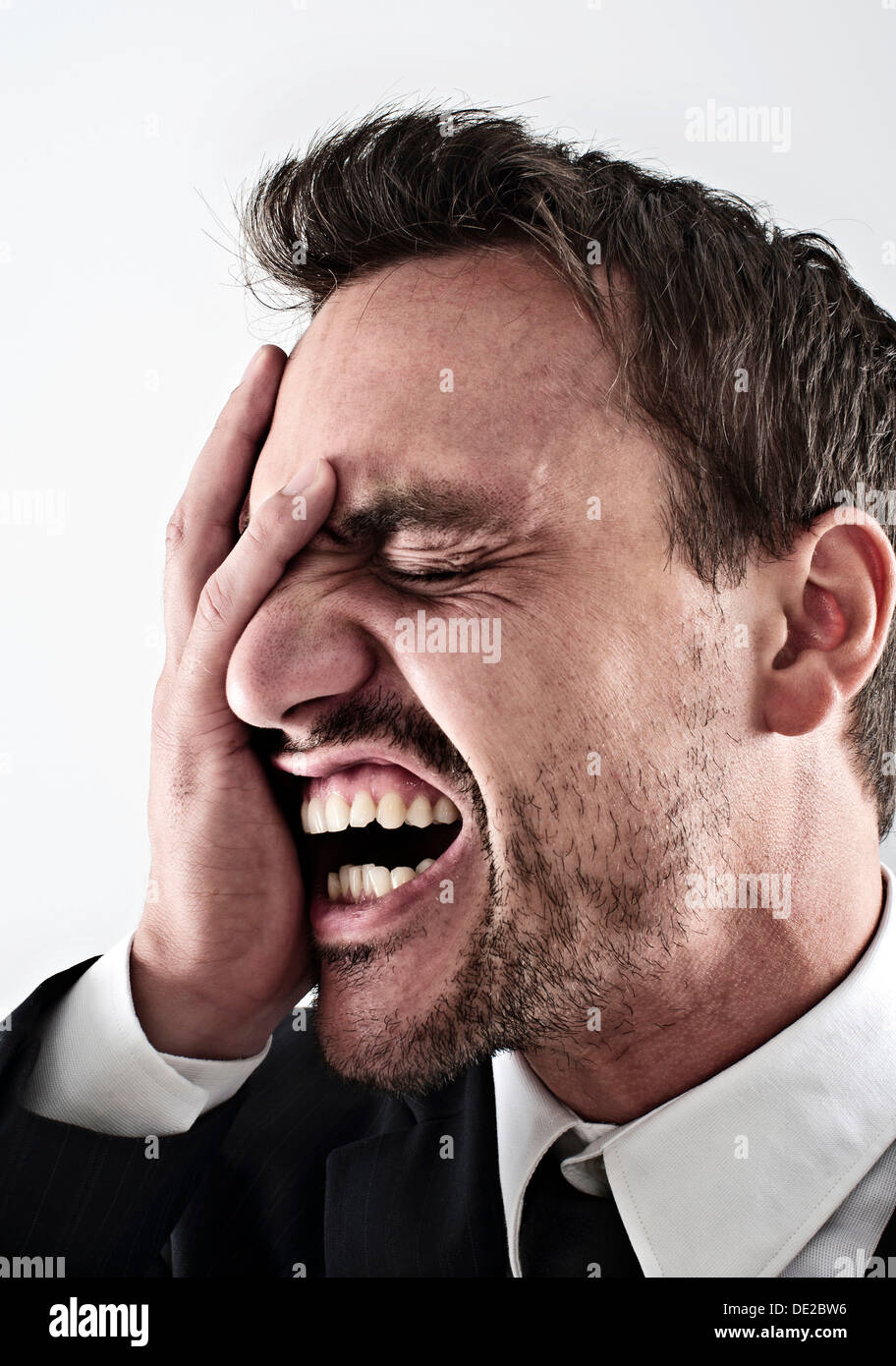 Desperate young man wearing a suit covering his face with his hand ...