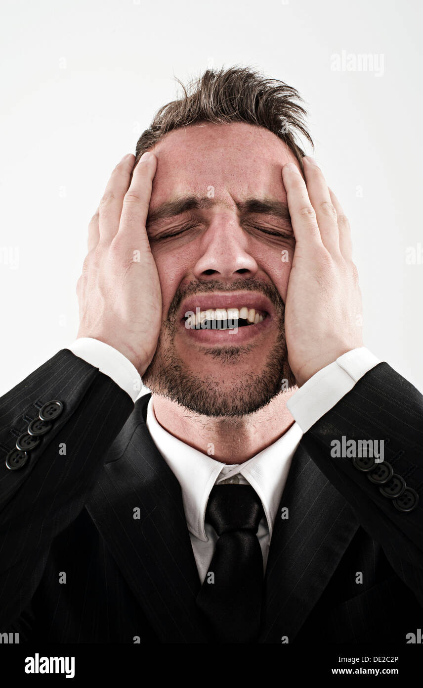 Desperate young man wearing a suit holding his hands to his face ...