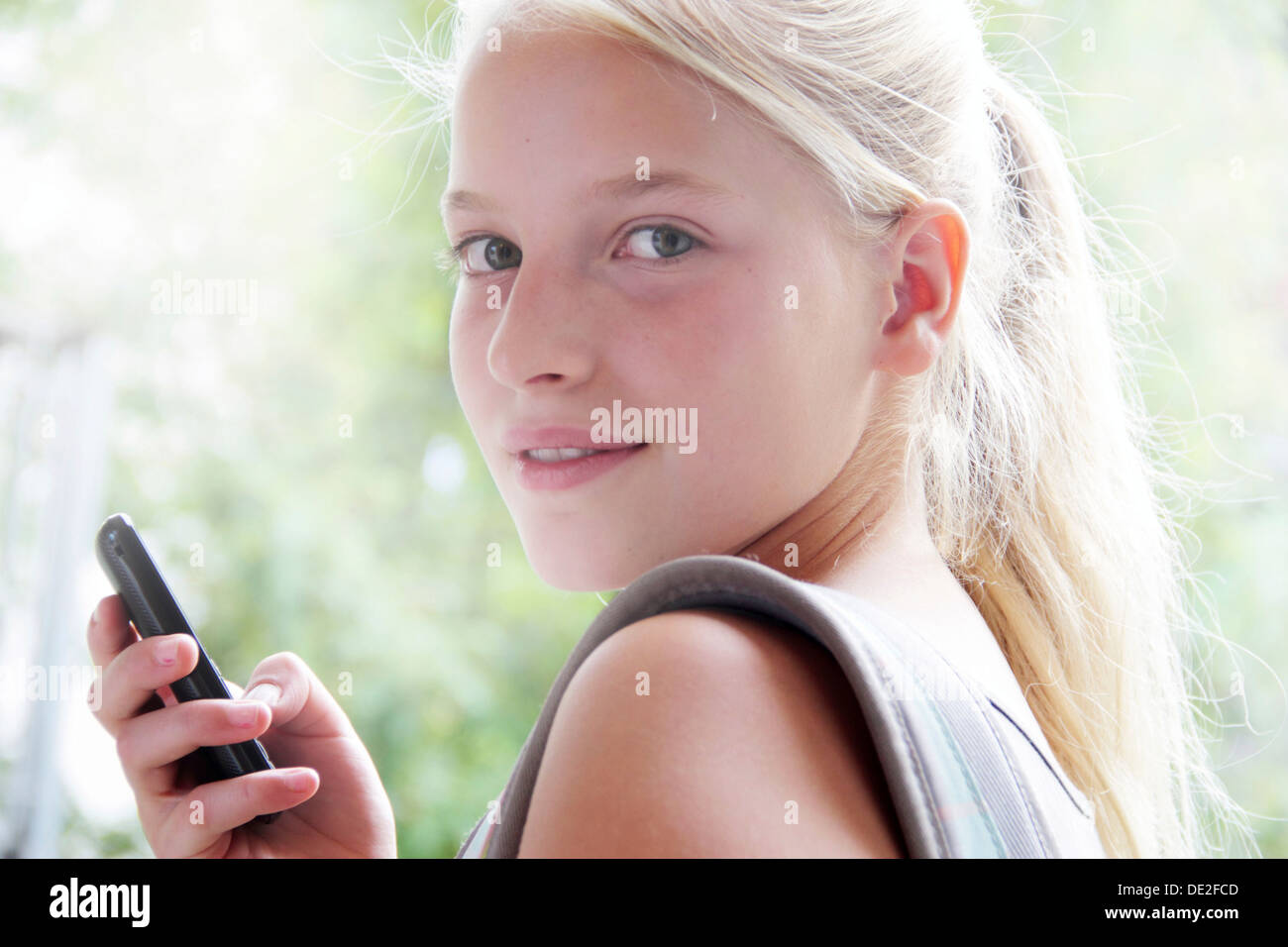 Girl looking towards the camera and holding a smartphone in her hand ...