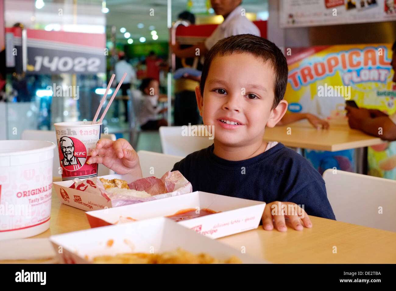 happy little boy of mixed race enjoying a chicken meal at kfc in malang ...