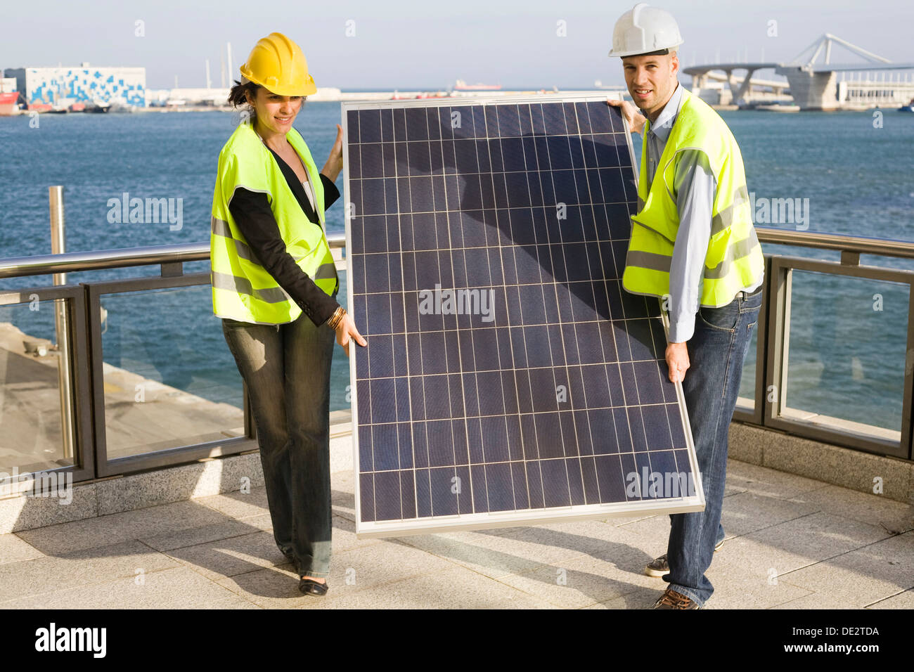 Two people in hard hats and protective jackets carrying a giant solar ...