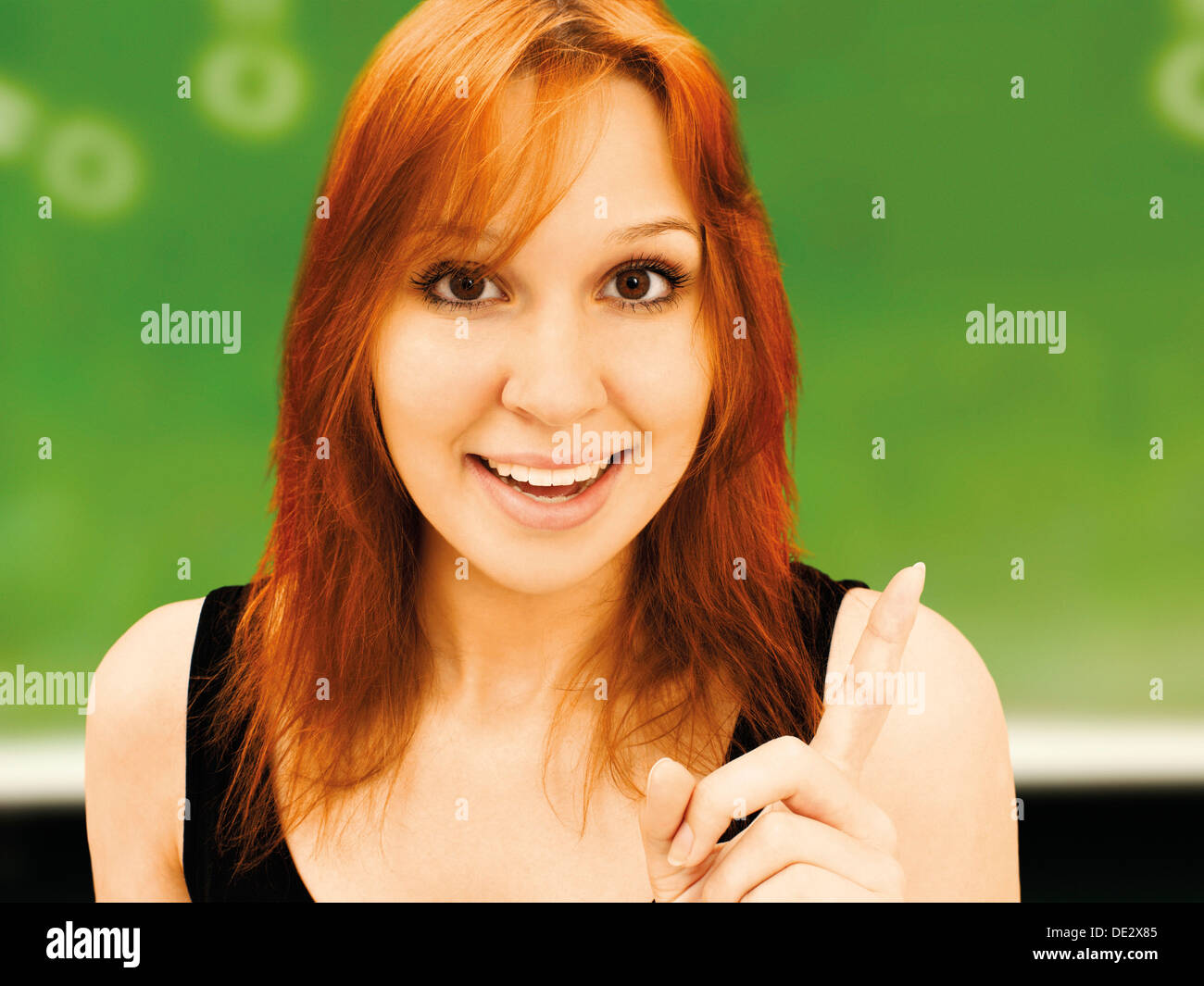 Young smiling teacher with a wagging finger, in front of a school board ...