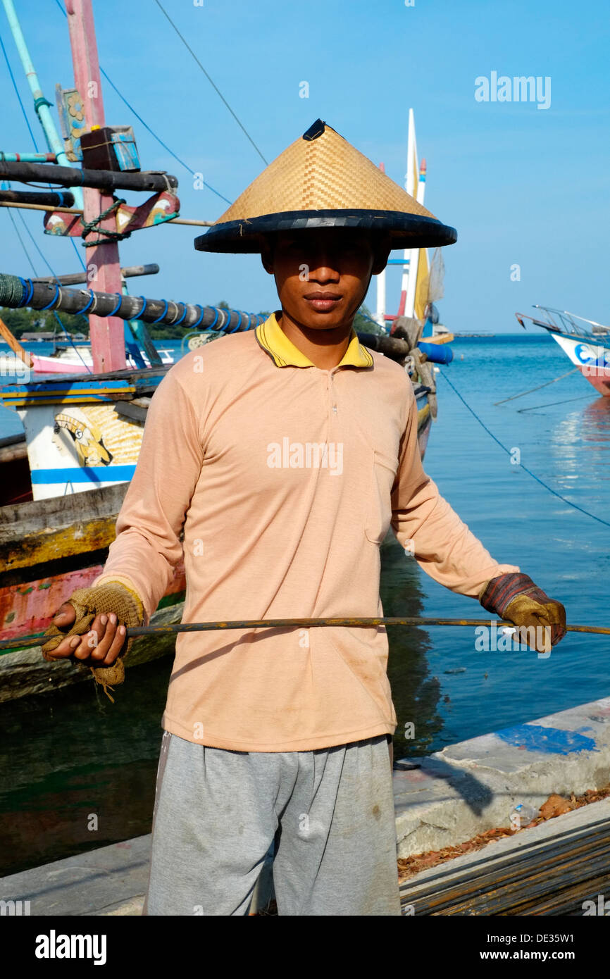 local worker in traditional pointed straw hat holding steel cable at ...