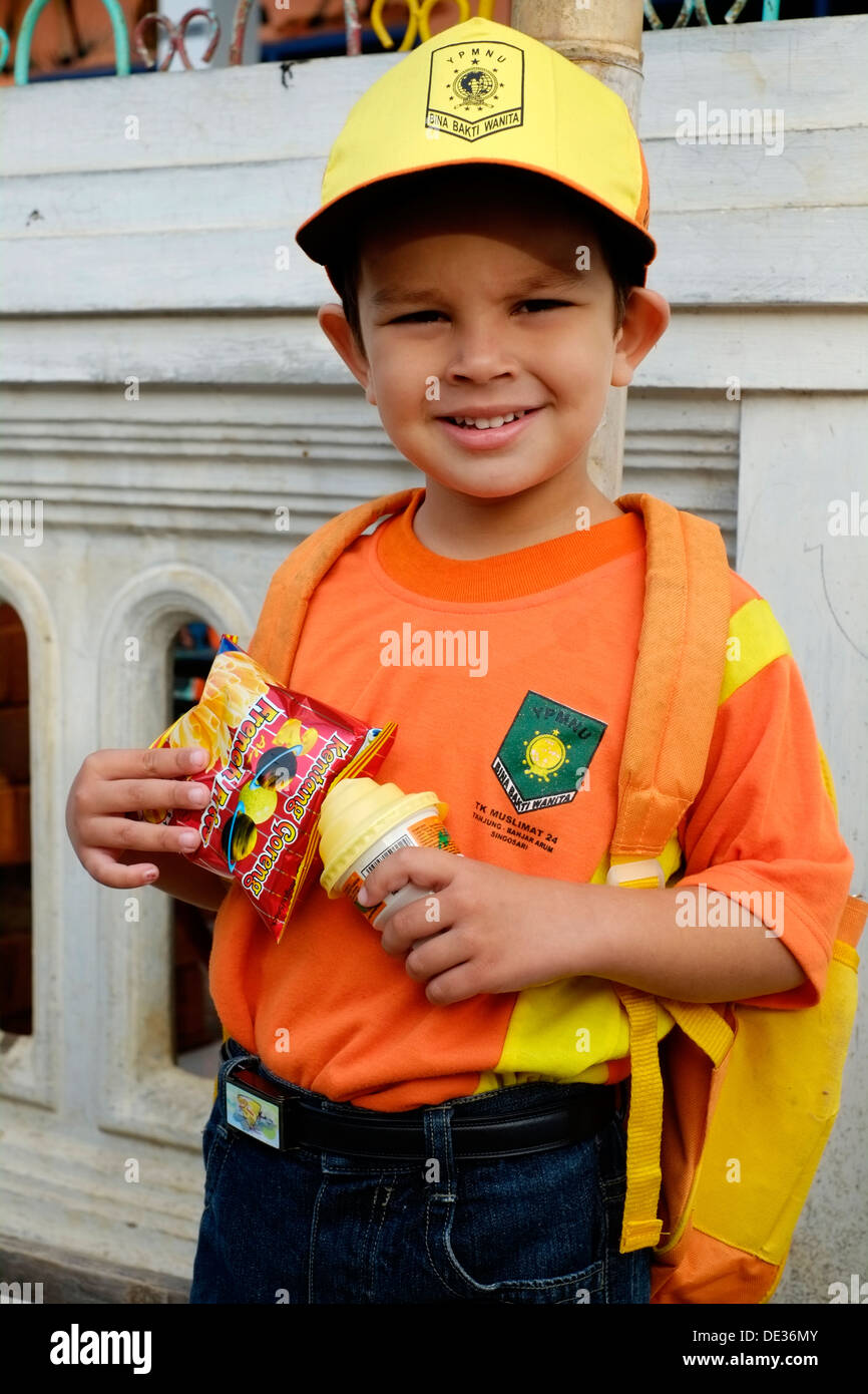 smiling young boy in his school uniform holding his snacks before going ...