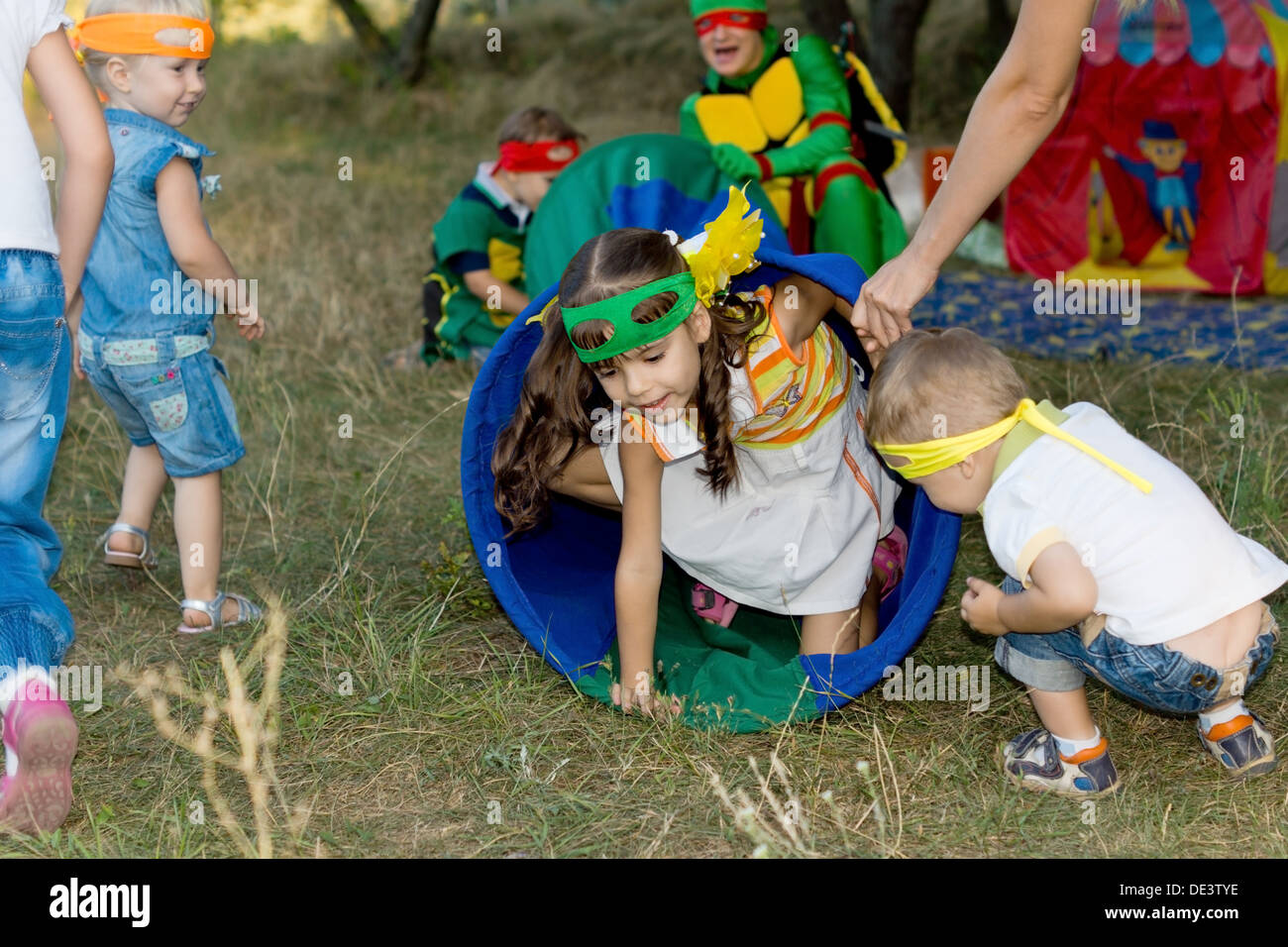Small children playing at a party crawling through a tube wearing ...