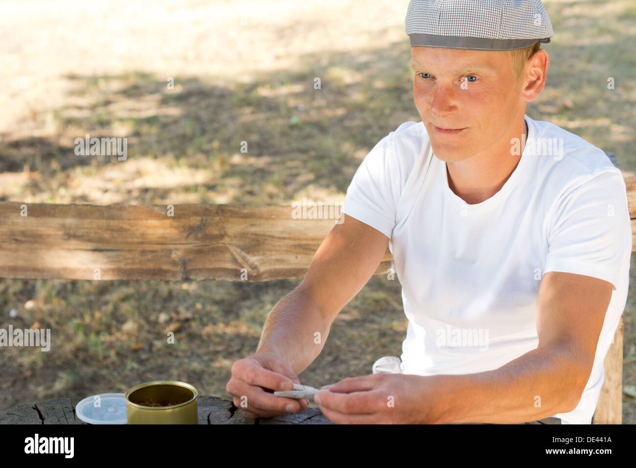 Smoker busy rolling a cigarette from a blend of ground tobacco in a jar ...