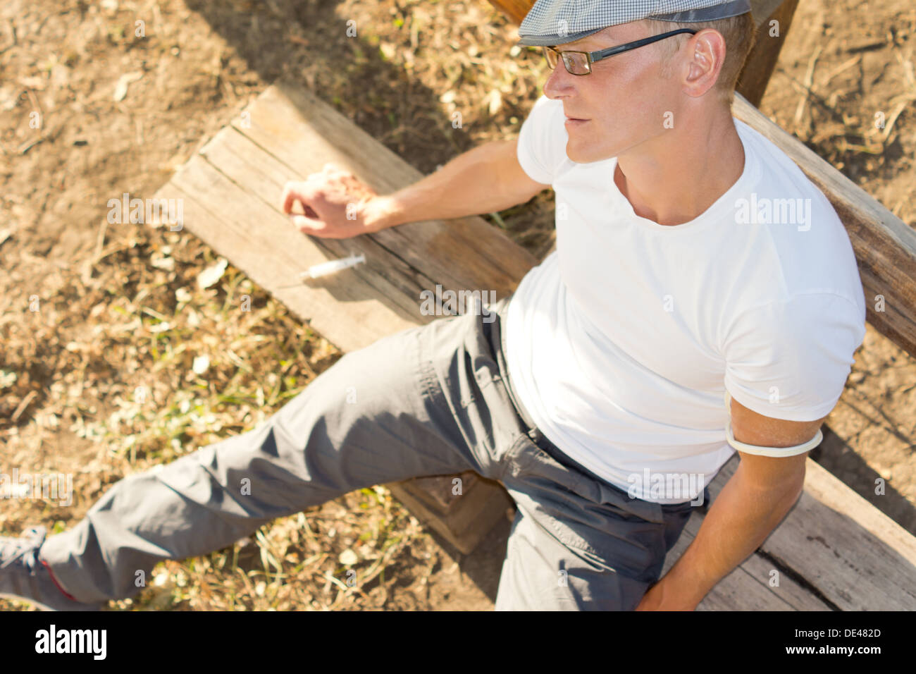 Heroin addict sitting on a bench in the park feeling sick in a warm ...