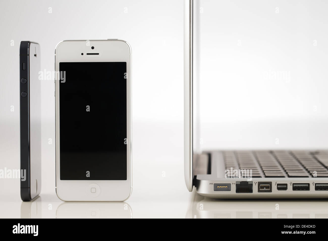Two modern smartphones laying on a shiny surface next to modern laptop ...