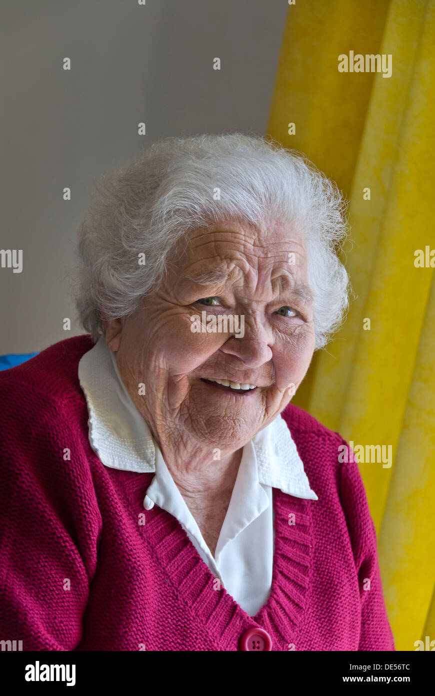 Portrait of happy smiling contented elderly lady in her light airy room ...