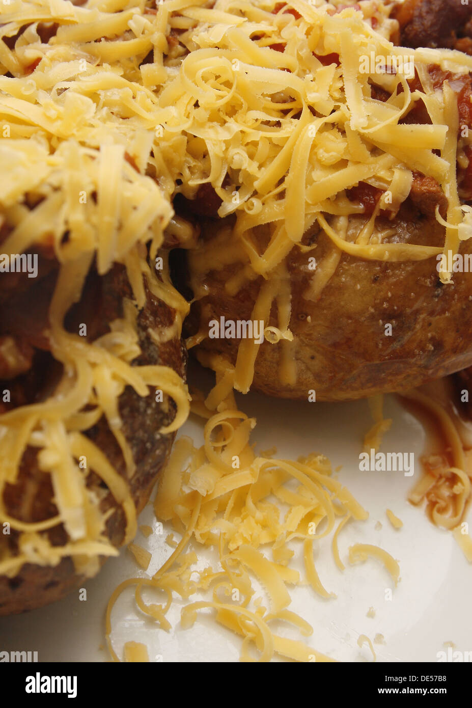 grated cheese, quorn chilli and jacket potato on white plate Stock ...
