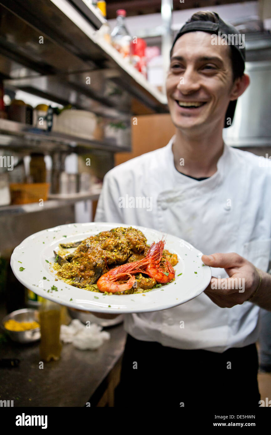 A chef preparing a black pasta and King Prawn dish in a restaurant ...