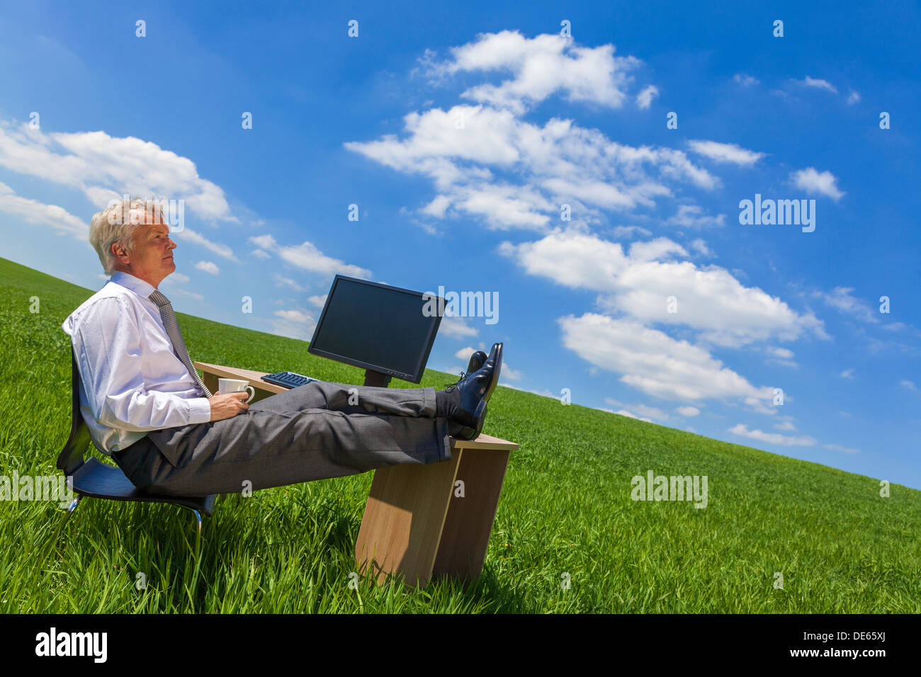 Man or male businessman relaxing feet up at a desk with a computer in a ...