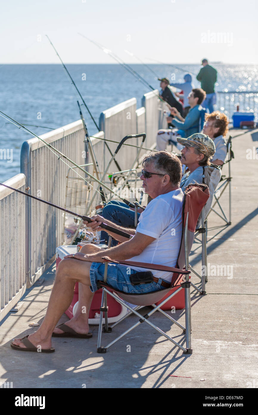 Adult men and women sitting and fishing from the fishing pier in the ...