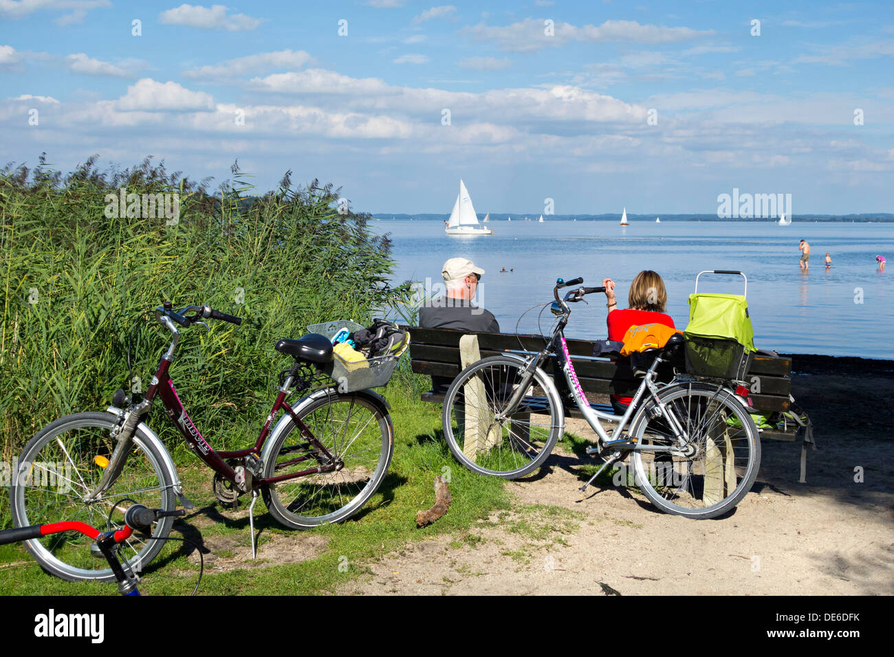 People sitting on a bench seat looking at lake, Chiemsee Chiemgau, Upper Bavaria Germany Stock ...