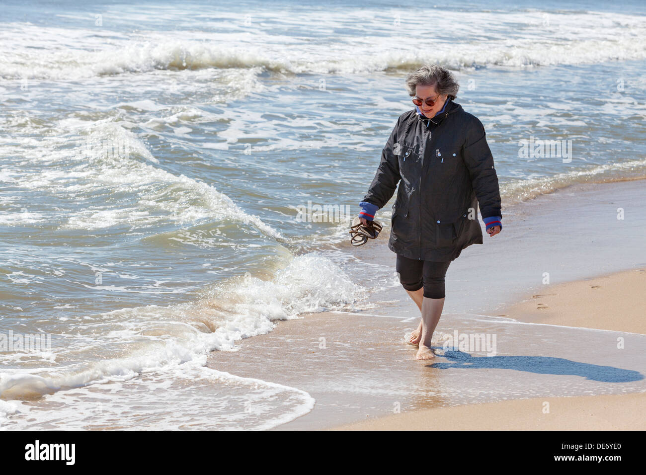 A woman walks along the ocean shore with waves Stock Photo - Alamy