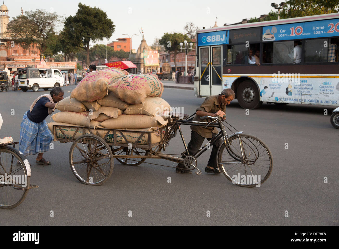 India, Rajasthan, Jaipur, two men pushing heavily loaded cycle trailer ...