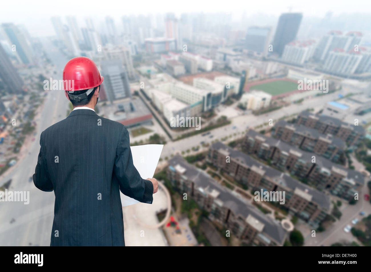 Rear view of architect looking comparing housing project with building ...