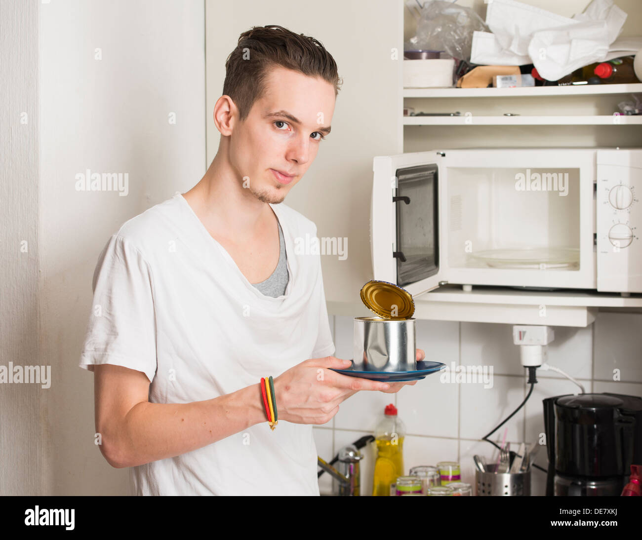 Young serious man standing in a messy kitchen holding plate with metal ...