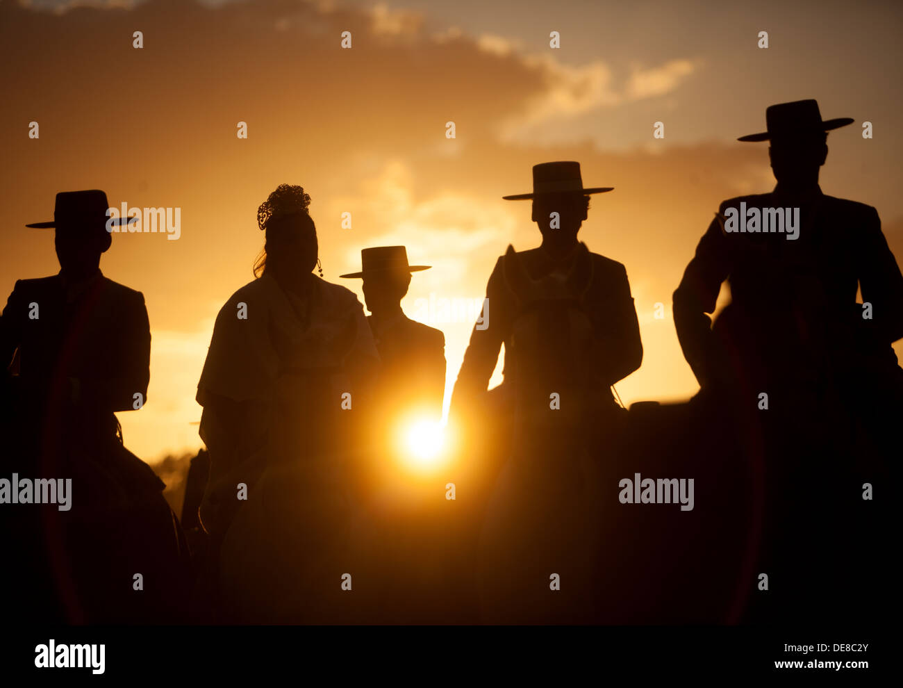 Pilgrims wearing Spanish hats ride their horses at sunset during the ...