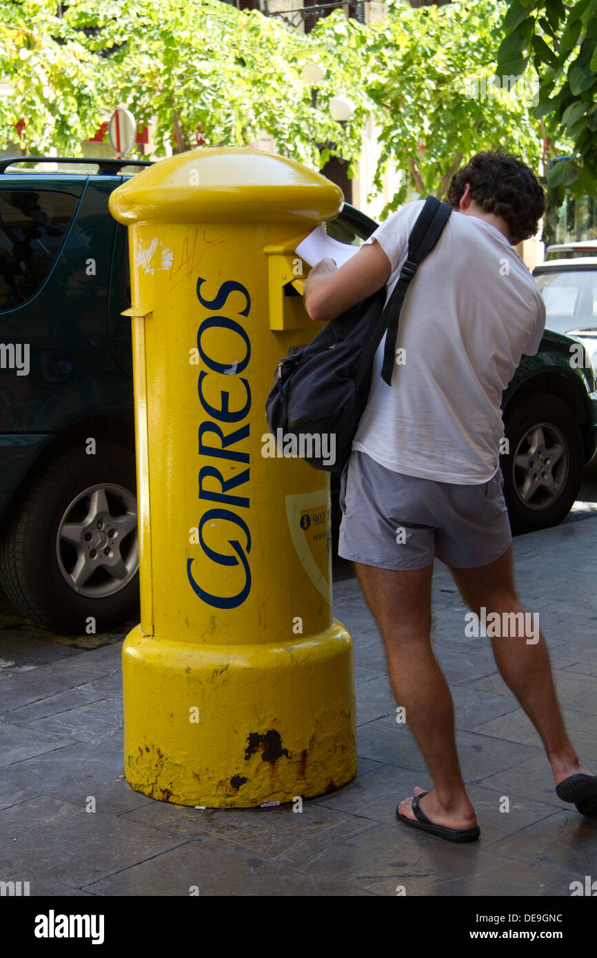 Man in shorts posting a letter into Spanish post box Stock Photo - Alamy