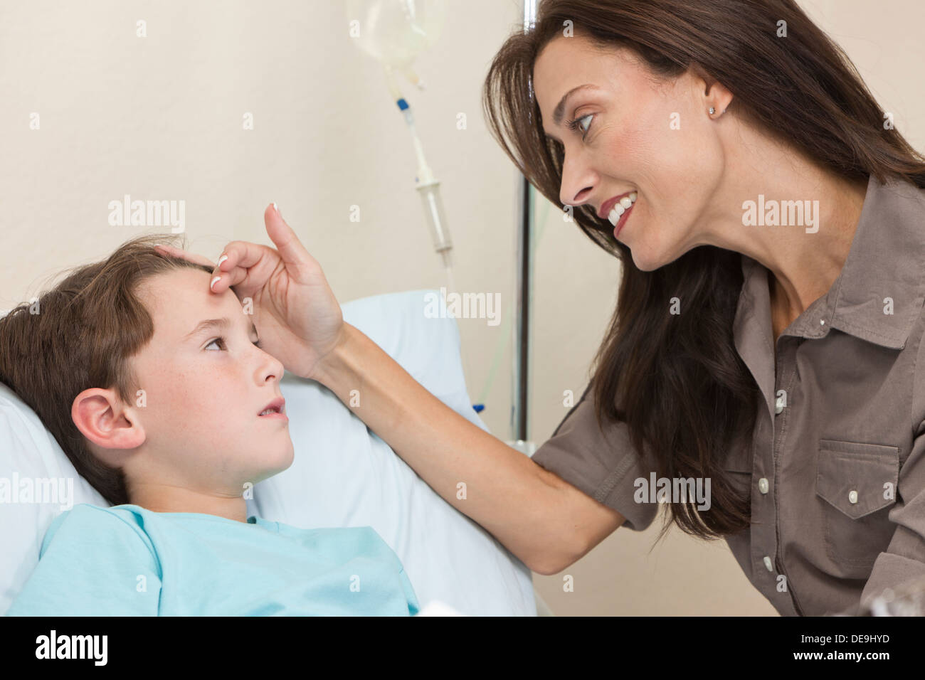 Young boy child in a hospital bed being comforted by his mother who is ...