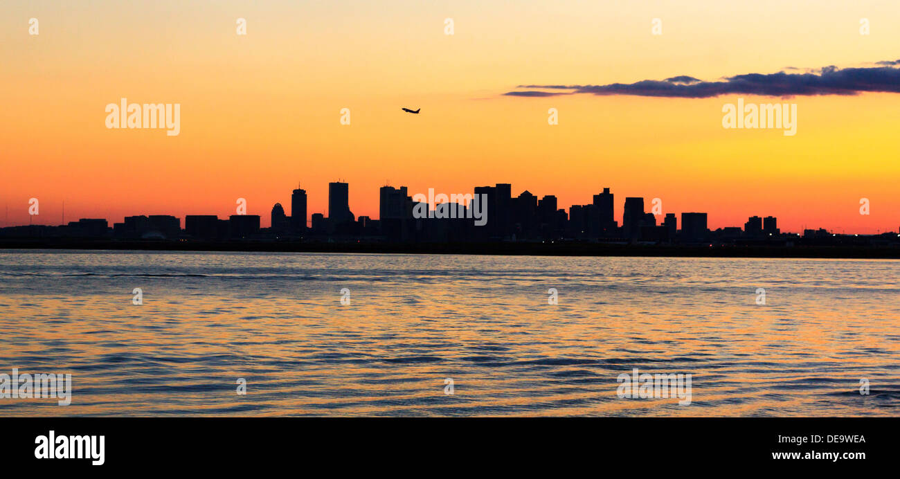 A photograph of the Boston skyline shot from the harbor at sunset ...