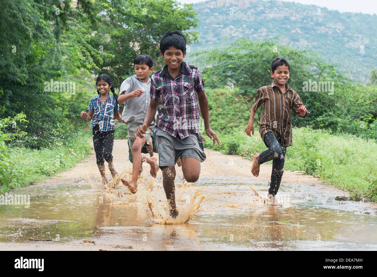 Rural Indian village children running through a muddy puddle. Andhra ...
