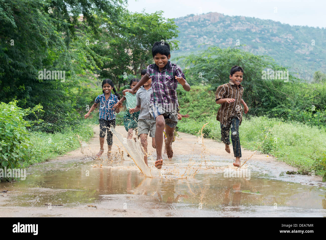 Rural Indian village children running through a muddy puddle. Andhra ...