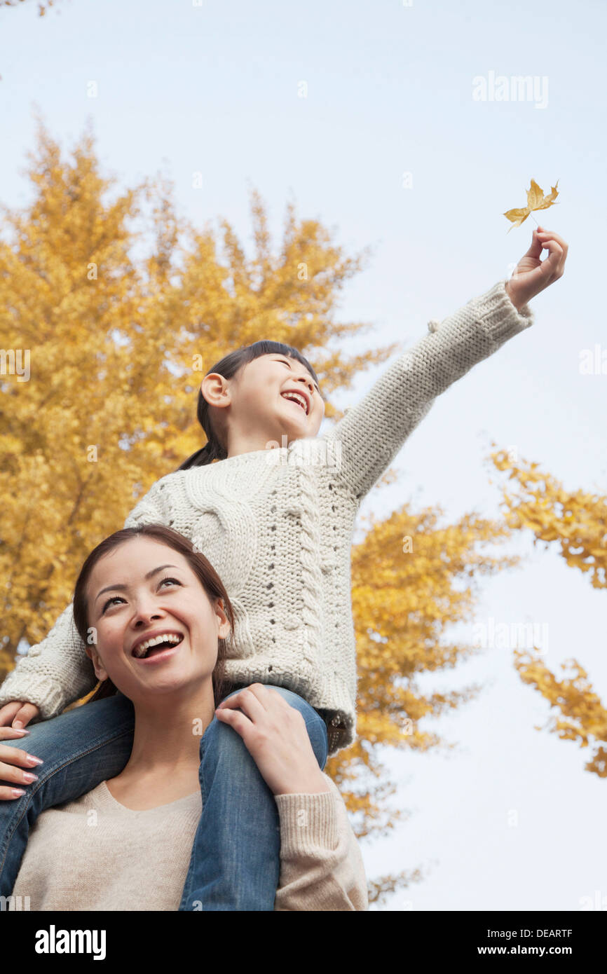 Daughter Riding Piggy-Back on Mother's Shoulders Enjoying Autumn Leaves Stock Photo - Alamy