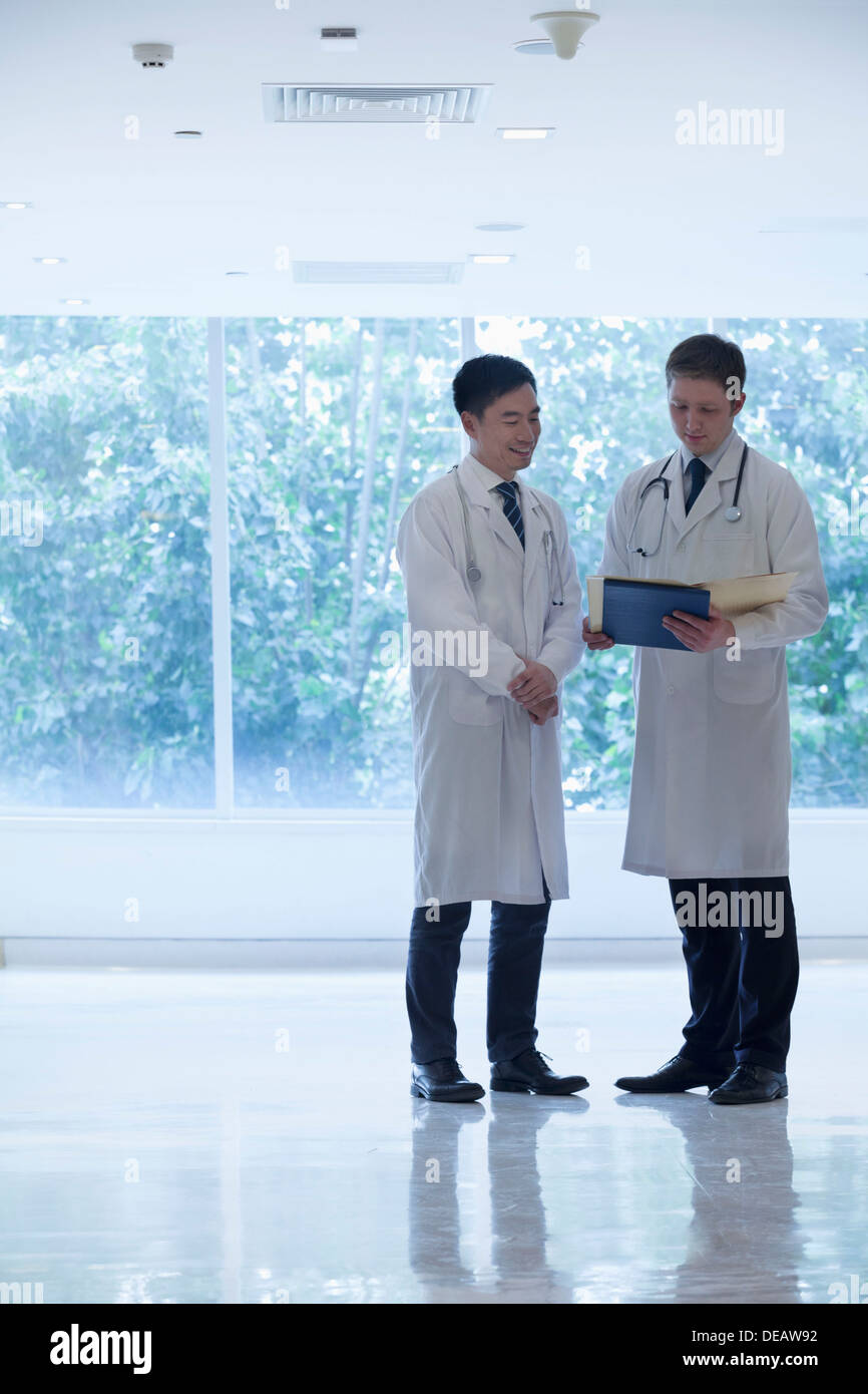 Two doctors standing, looking down, and consulting over medical record ...
