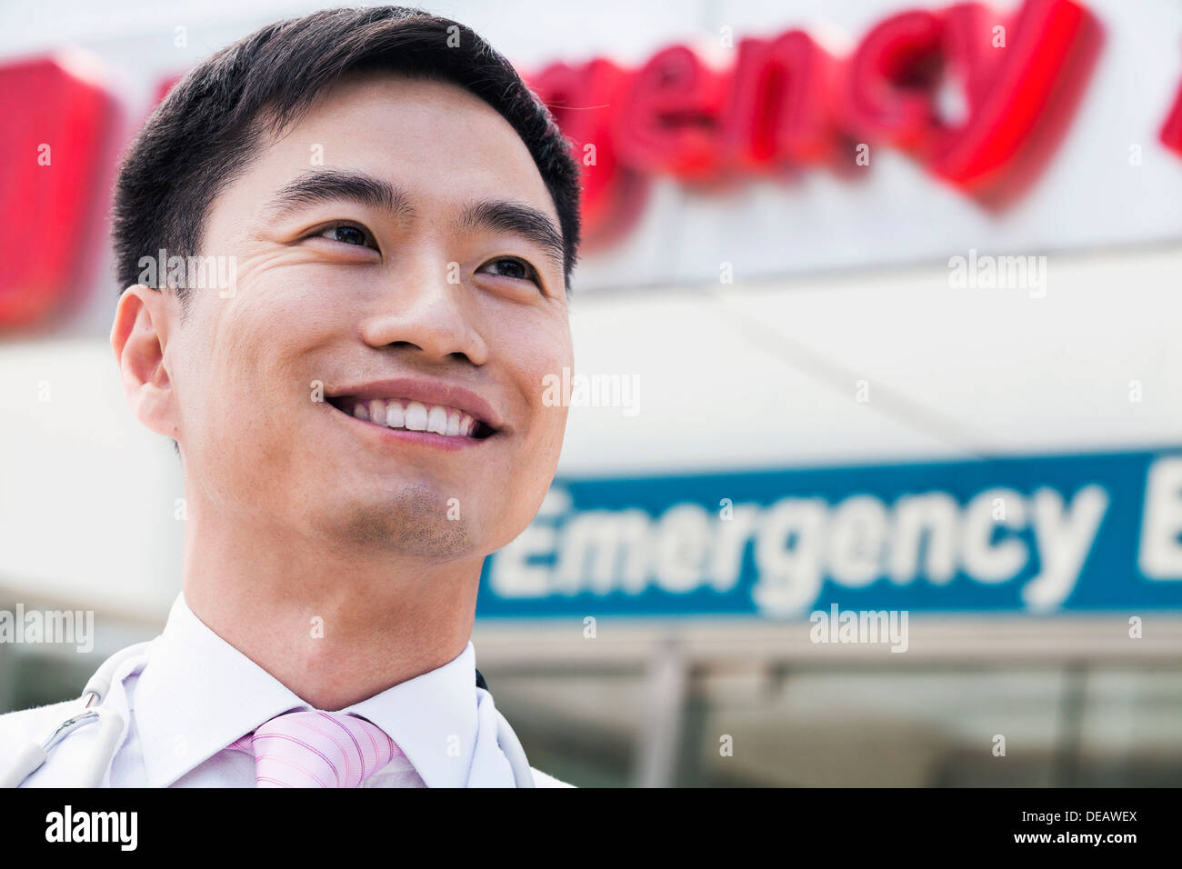 Portrait of smiling doctor outside of the hospital, emergency room sign ...