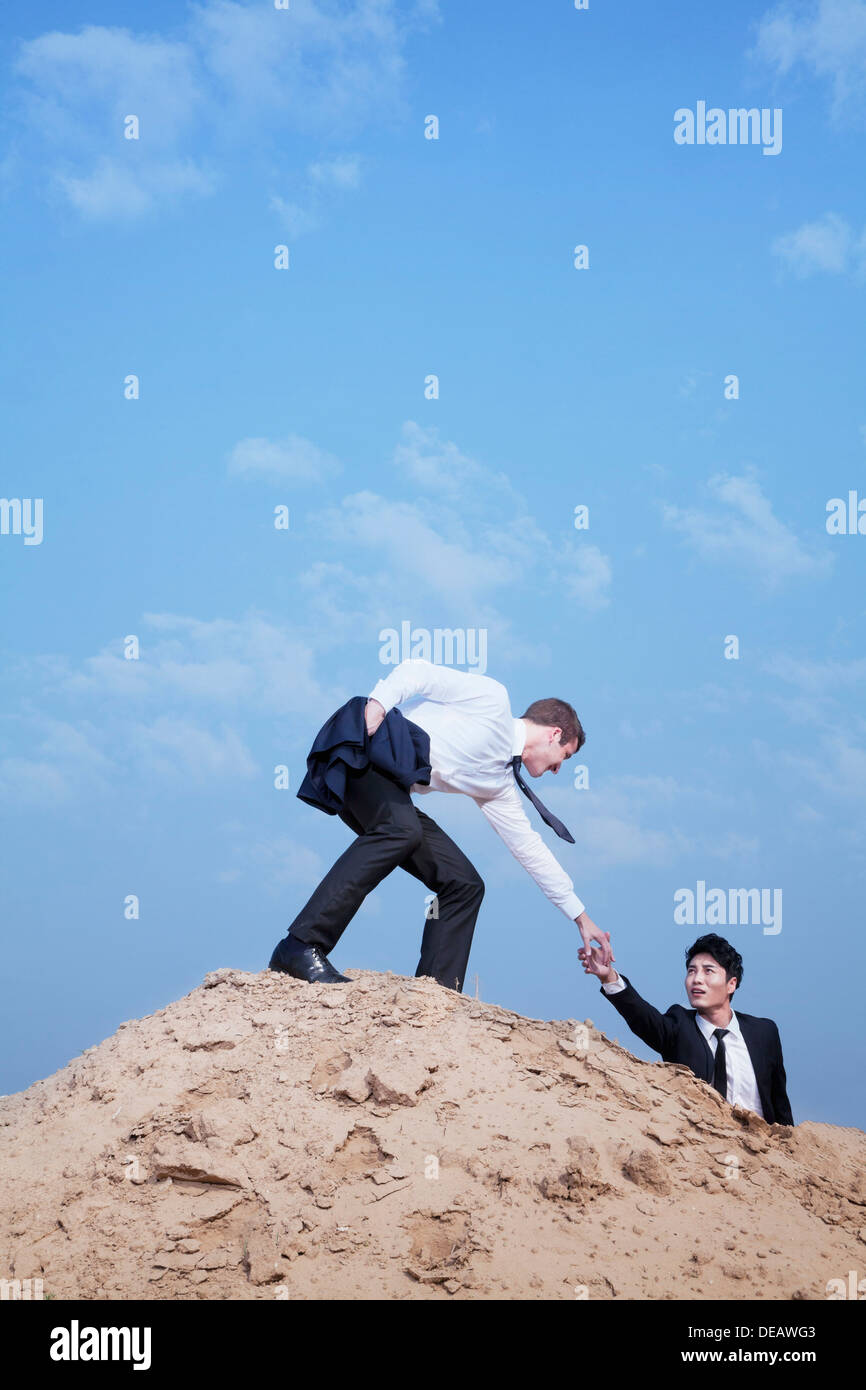 Young businessman helping another businessman get to the top of the ...