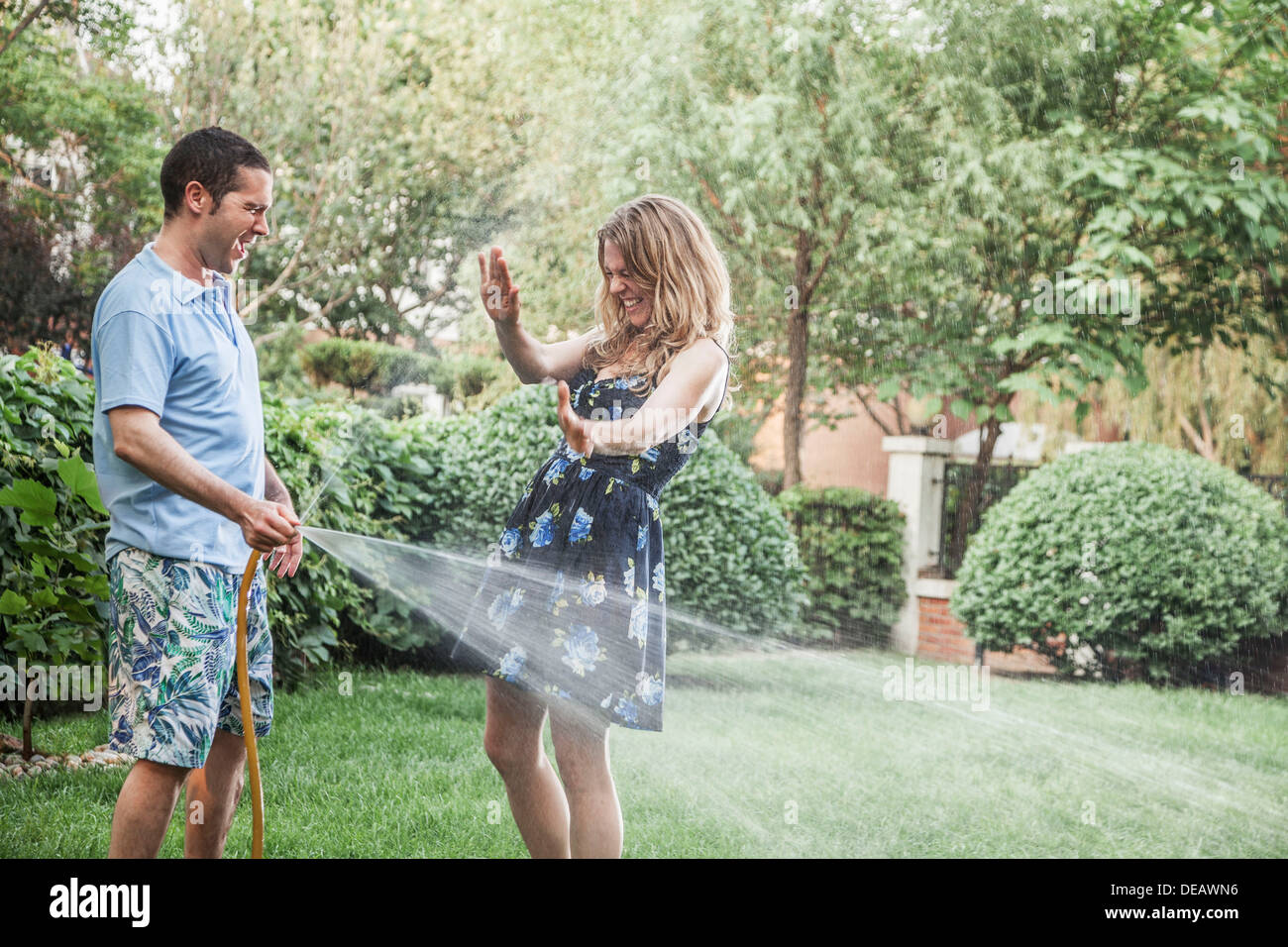 Couple playing with a garden hose and spraying each other outside in ...