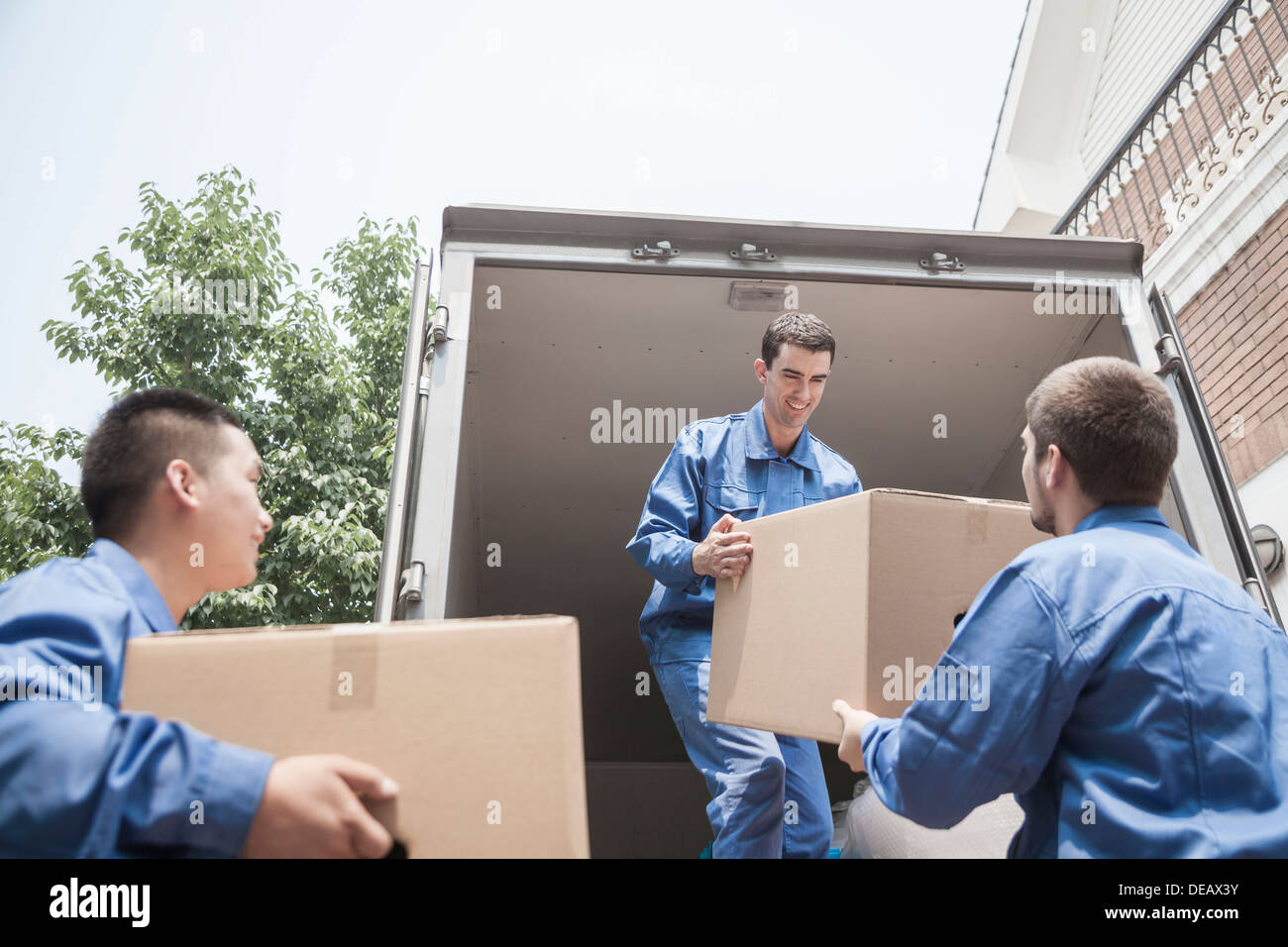 Movers unloading a moving van, passing a cardboard box Stock Photo - Alamy
