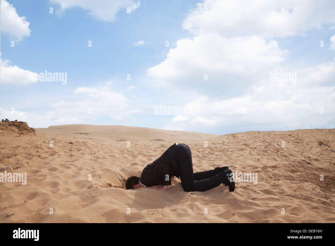 Young businessman kneeling with his head in a hole in the sand Stock ...
