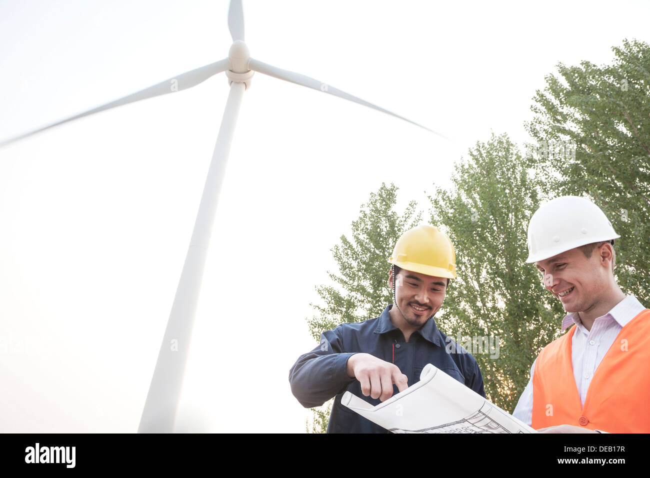 Two young male engineers in hardhats looking down at a blueprint in ...