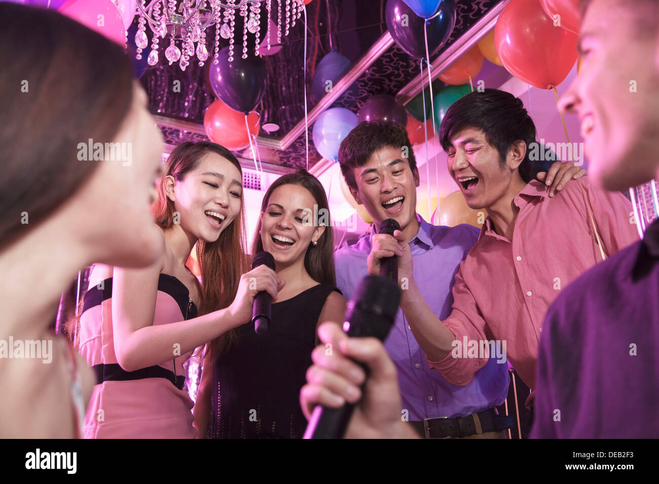 Group of friends holding microphones in a nightclub and singing ...
