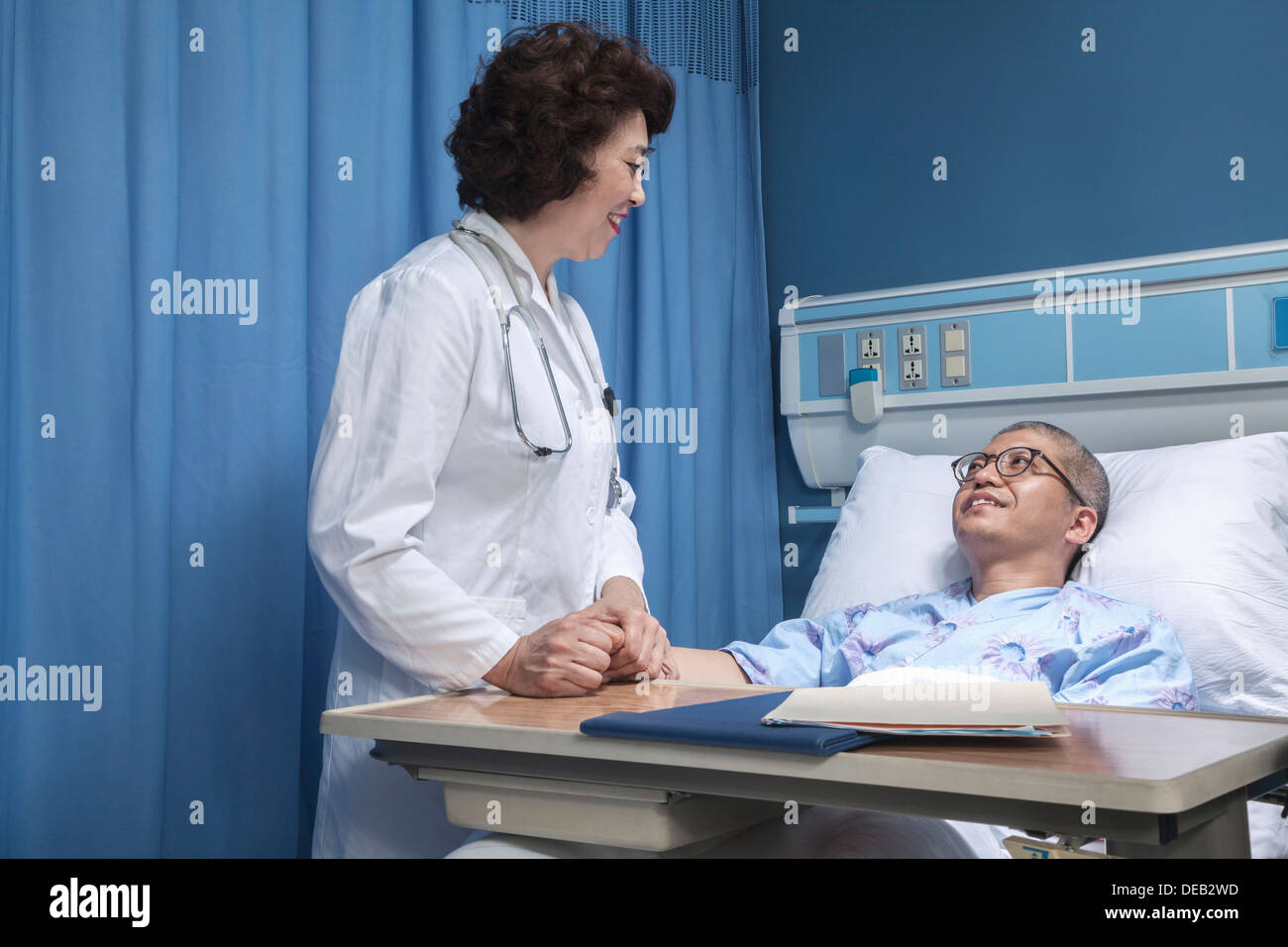 Smiling doctor checking up on a patient lying down in a hospital bed ...