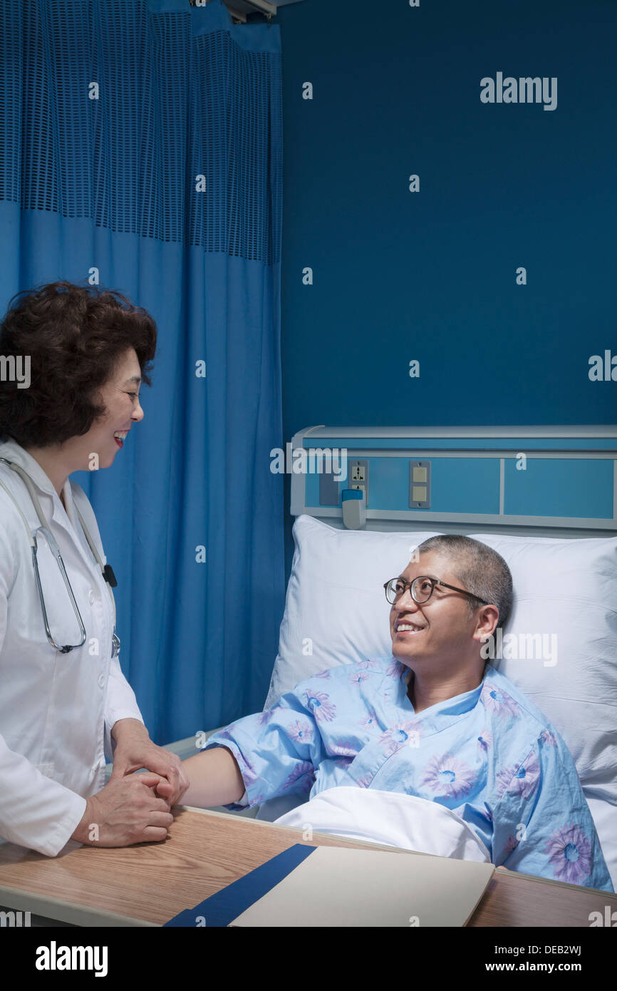 Smiling doctor checking up on a patient lying down in a hospital bed ...