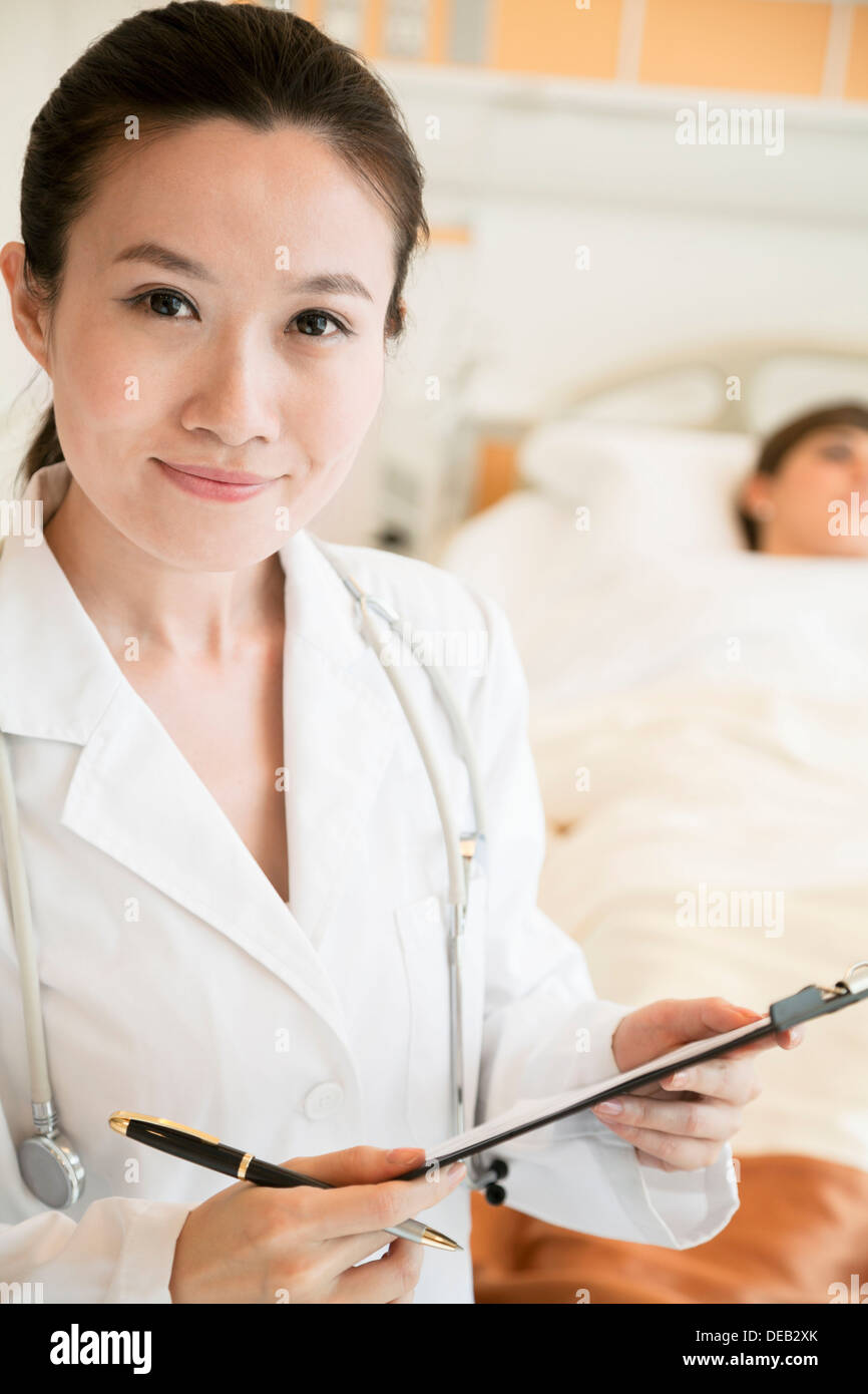 Portrait of smiling doctor holding a medical chart with patient lying ...