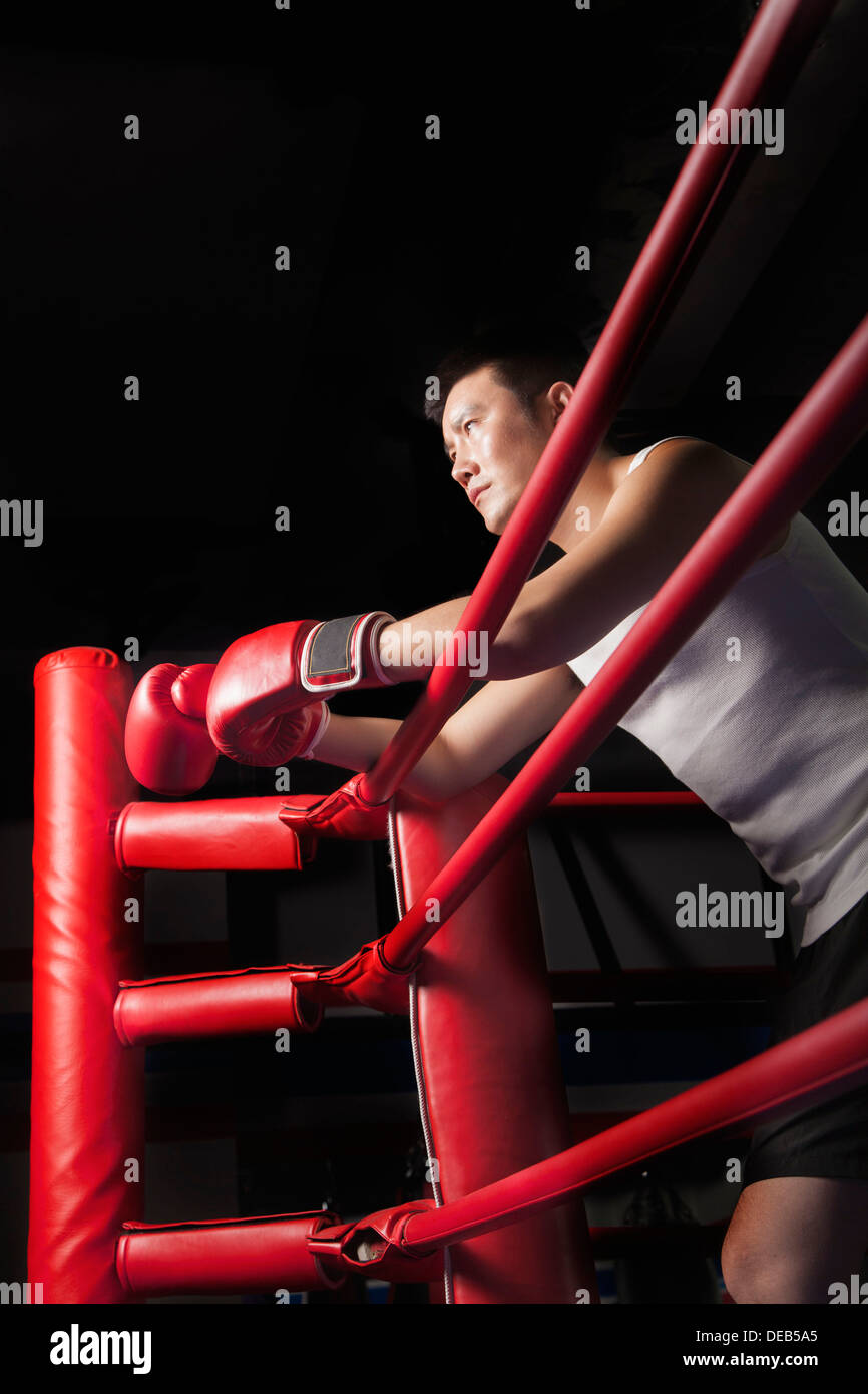 Serious male boxer resting his elbows on the ring side, low angle view ...